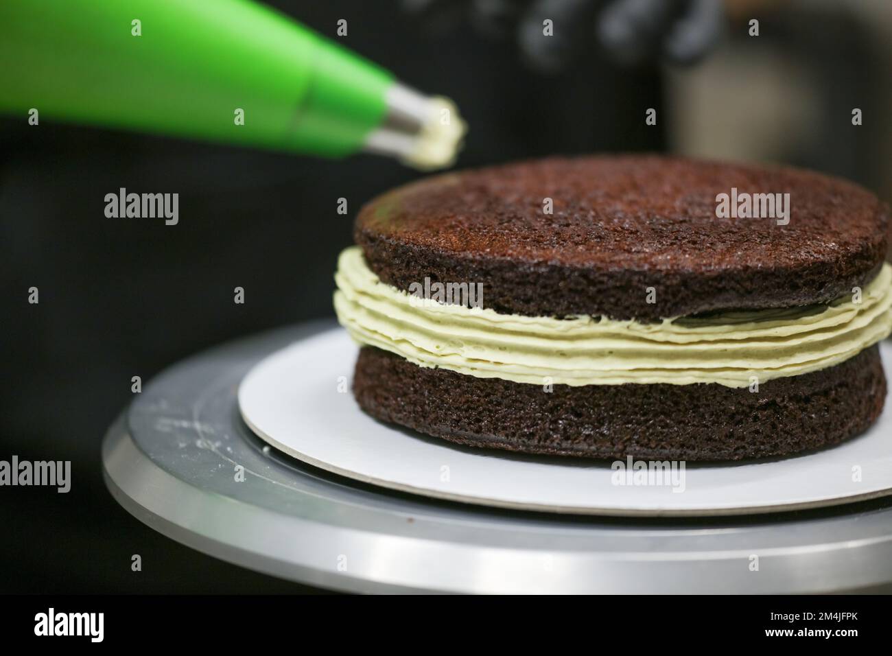 cake chef designer using pistachio cream filling piping bag on layered ...