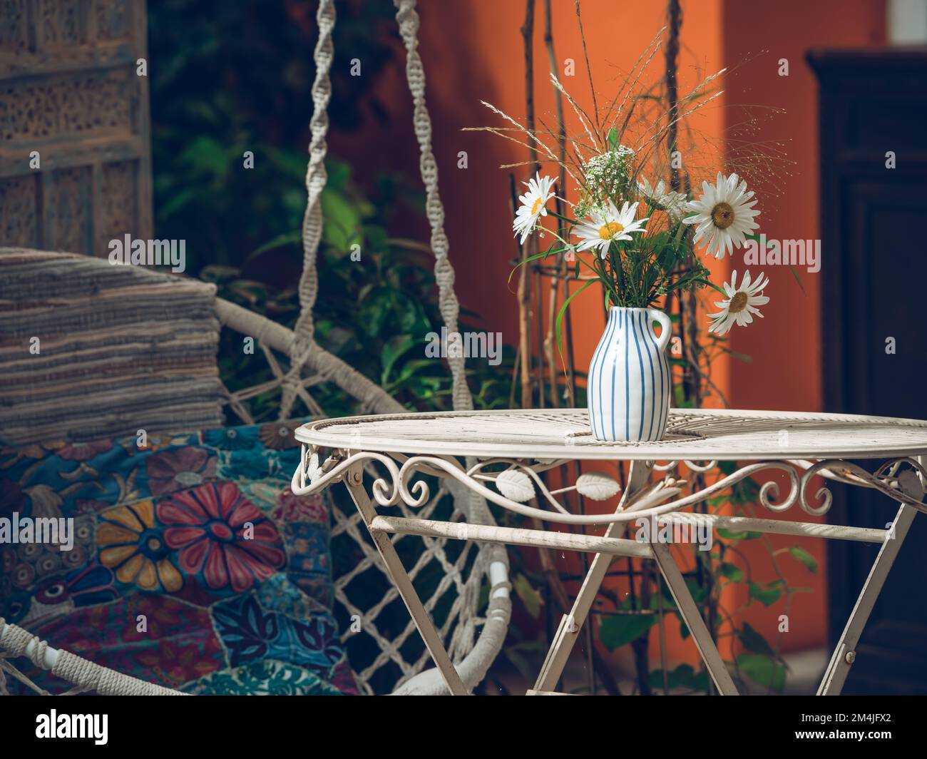 Interior of veranda. Hanging wicker chair, flowers on table. Close-up ...