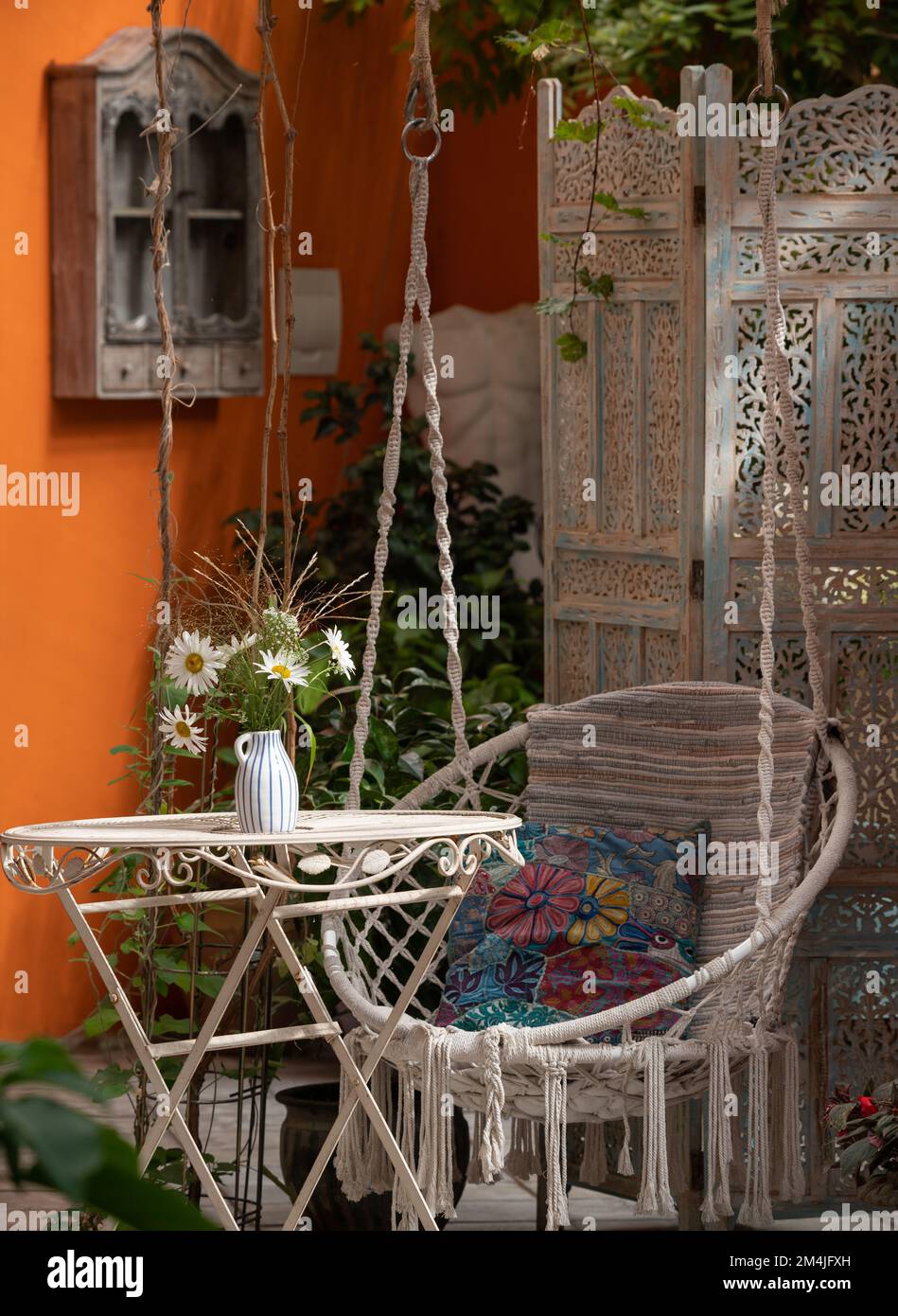 Interior of veranda. Hanging wicker chair, flowers on table. Close-up ...