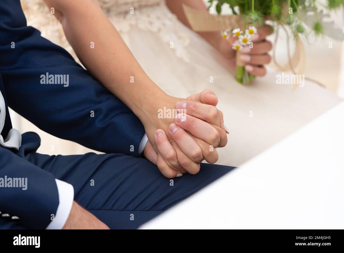 bride and groom holding hands, sitting in front of the altar. Closeup ...