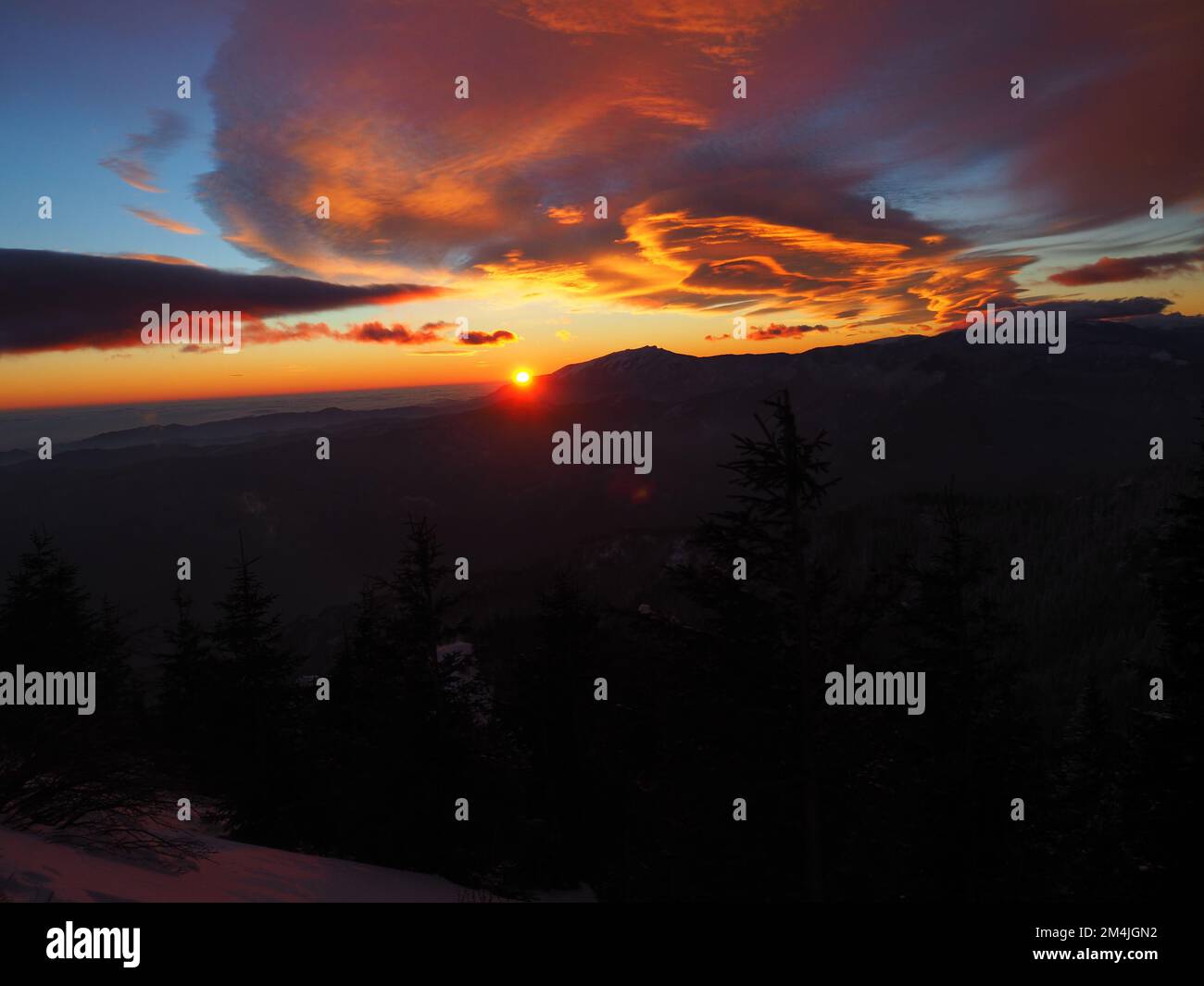 The silhouettes of trees and mountains before the shaded sunset sky on ...