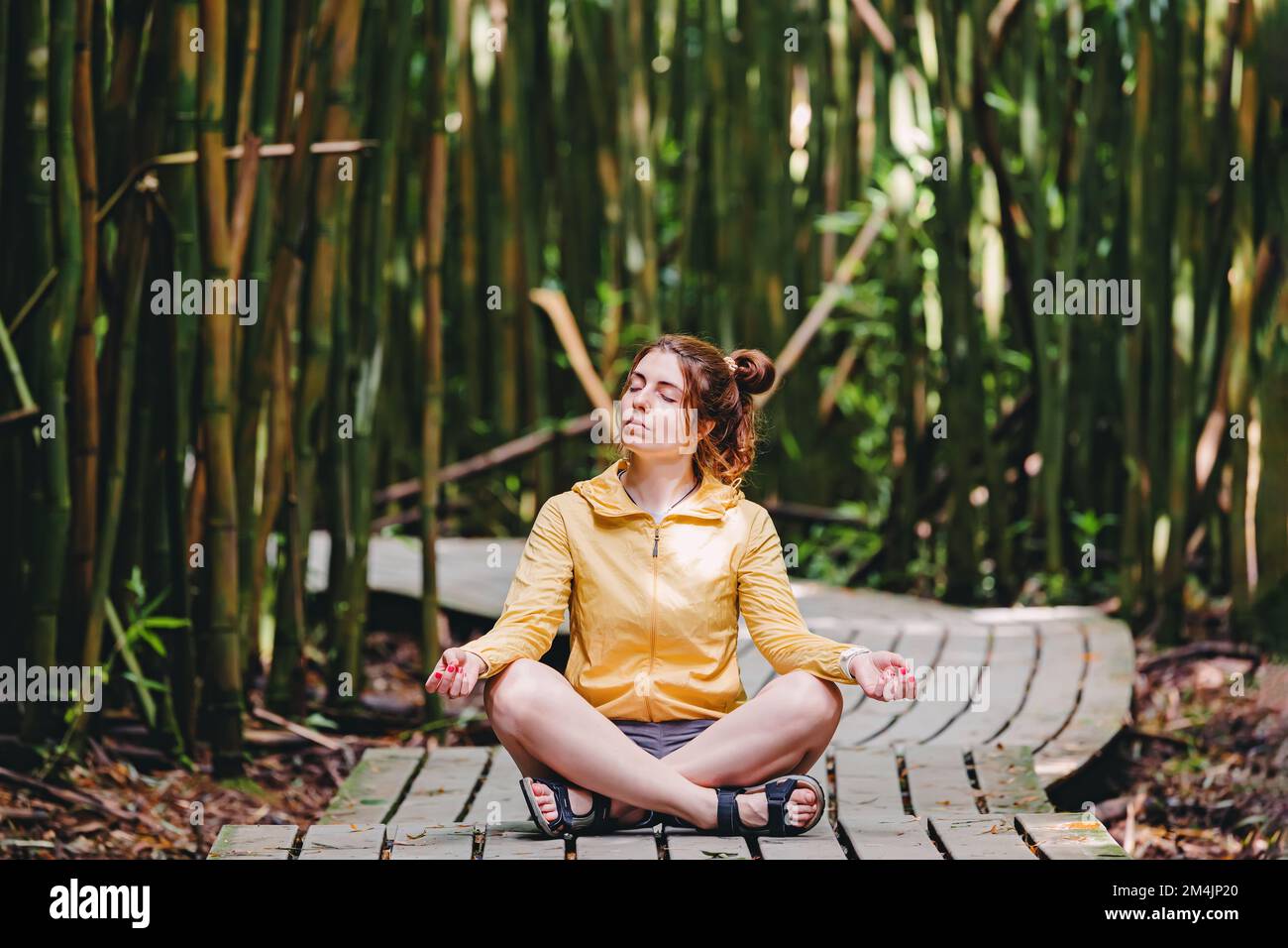 Young woman relaxing among the bamboo tress. Sitting in meditation pose ...