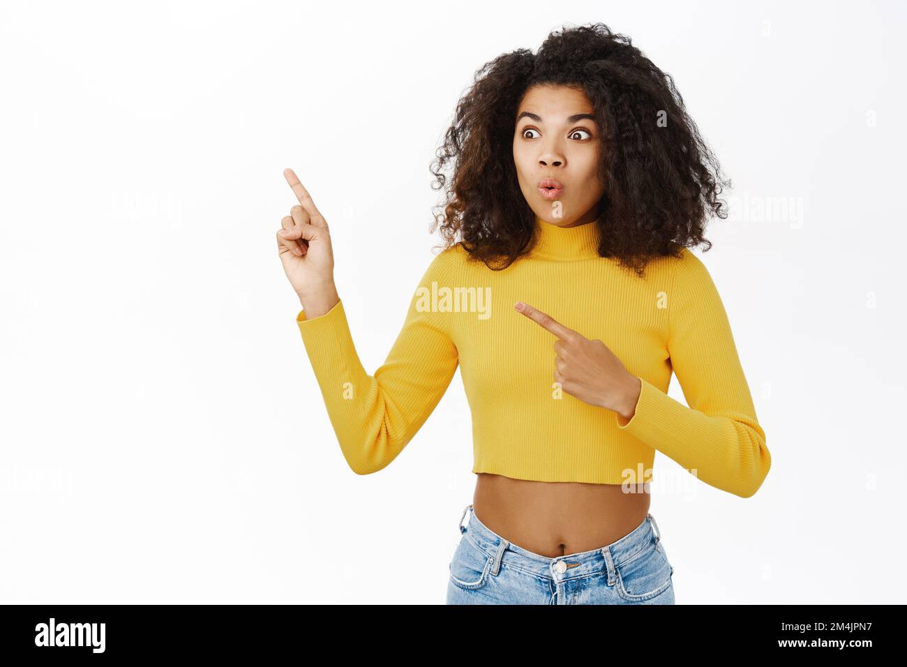 Portrait of surprised young black woman, pointing and looking amazed ...