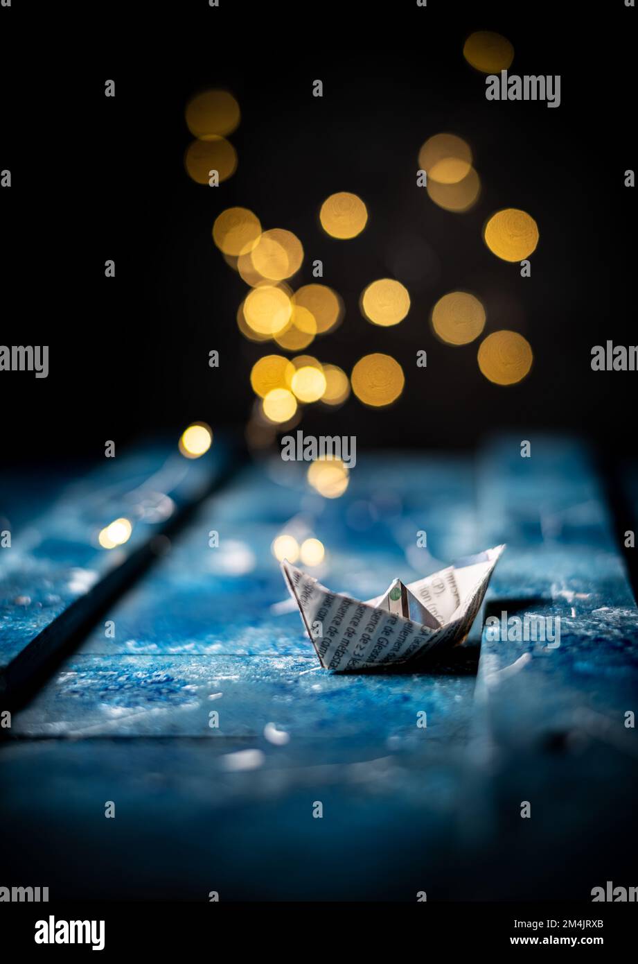 close-up of an origami boat on a dark blue wooden background with bokeh ...
