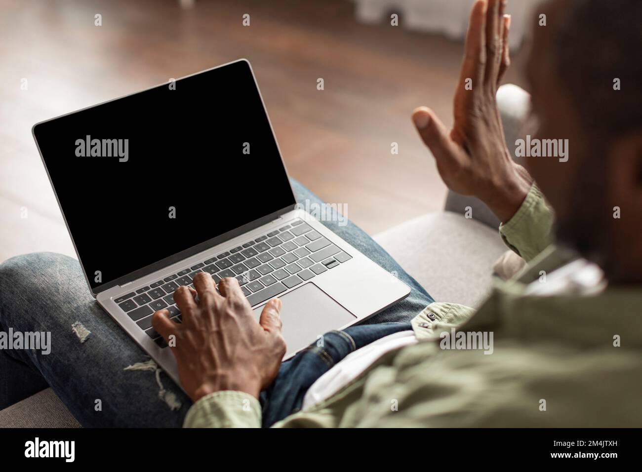 Happy adult black man using computer with blank screen, waving hand at webcam, have meeting, sit ...