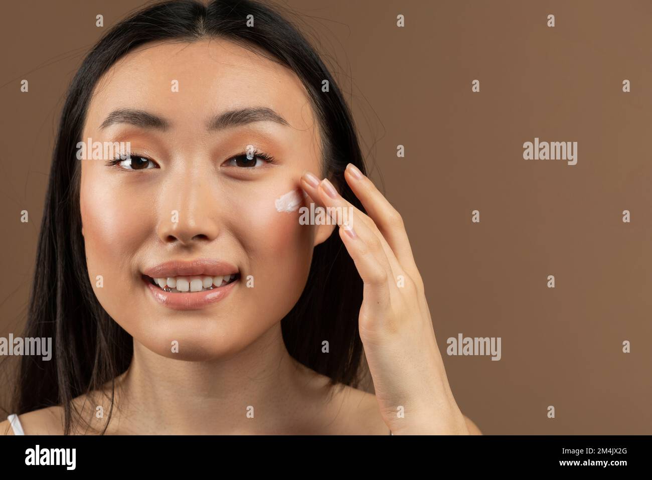Portrait of asian lady applying anti-aging or moisturising face cream ...