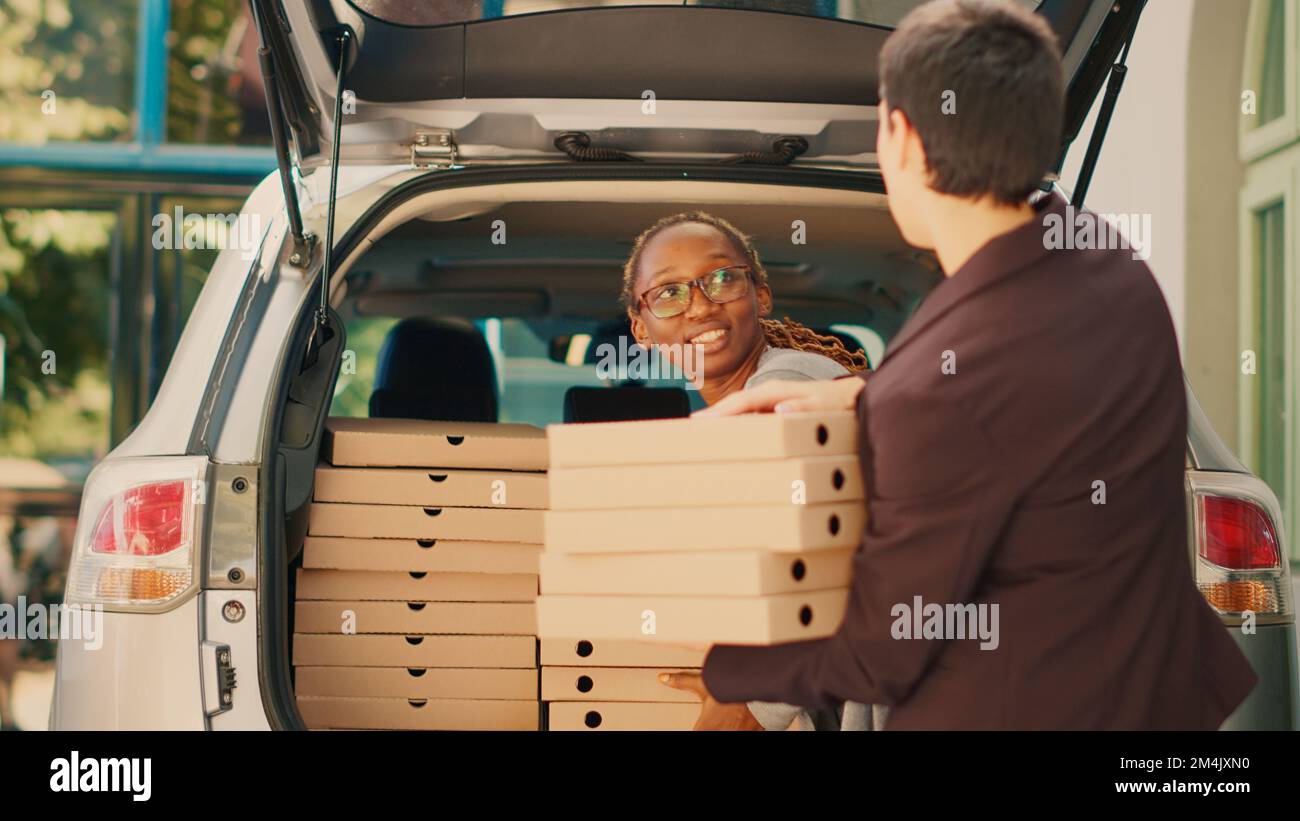 Woman pizzeria courier delivering big fastfood order from vehicle trunk ...