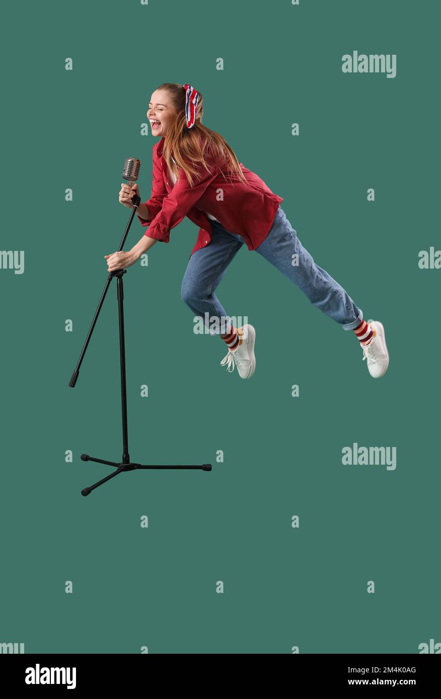 Young female singer with microphone jumping on green background Stock ...