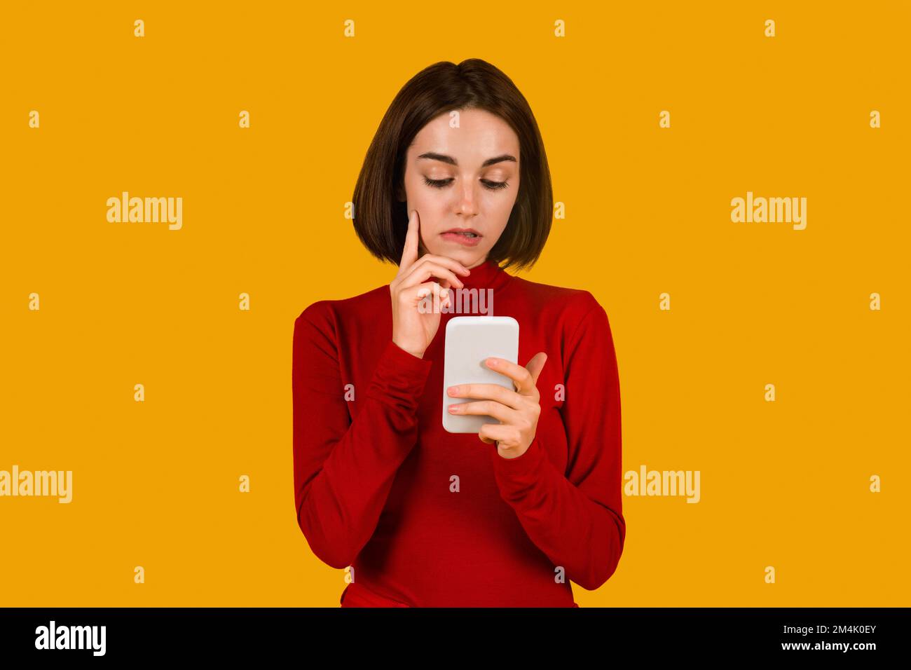Curious attractive lady looking at cell phone screen, orange background ...