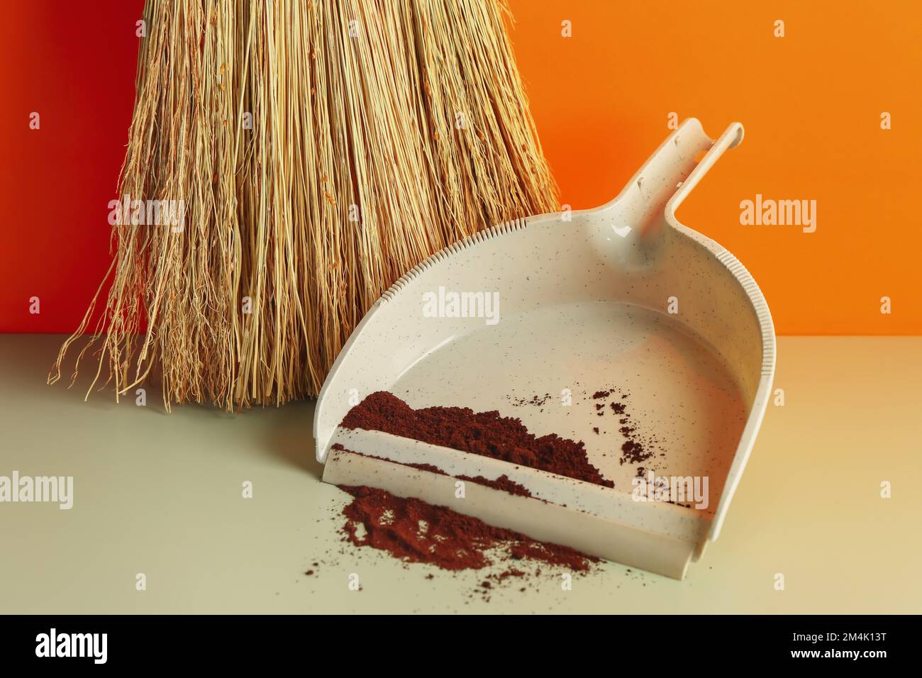 Dustpan with scattered coffee and broom on floor near color wall ...
