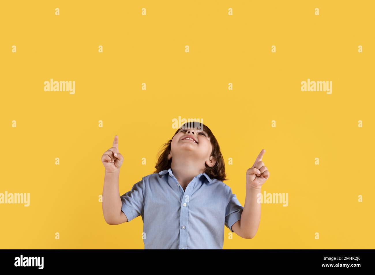 Cute little boy looking upward and pointing with both hands, enjoying ...