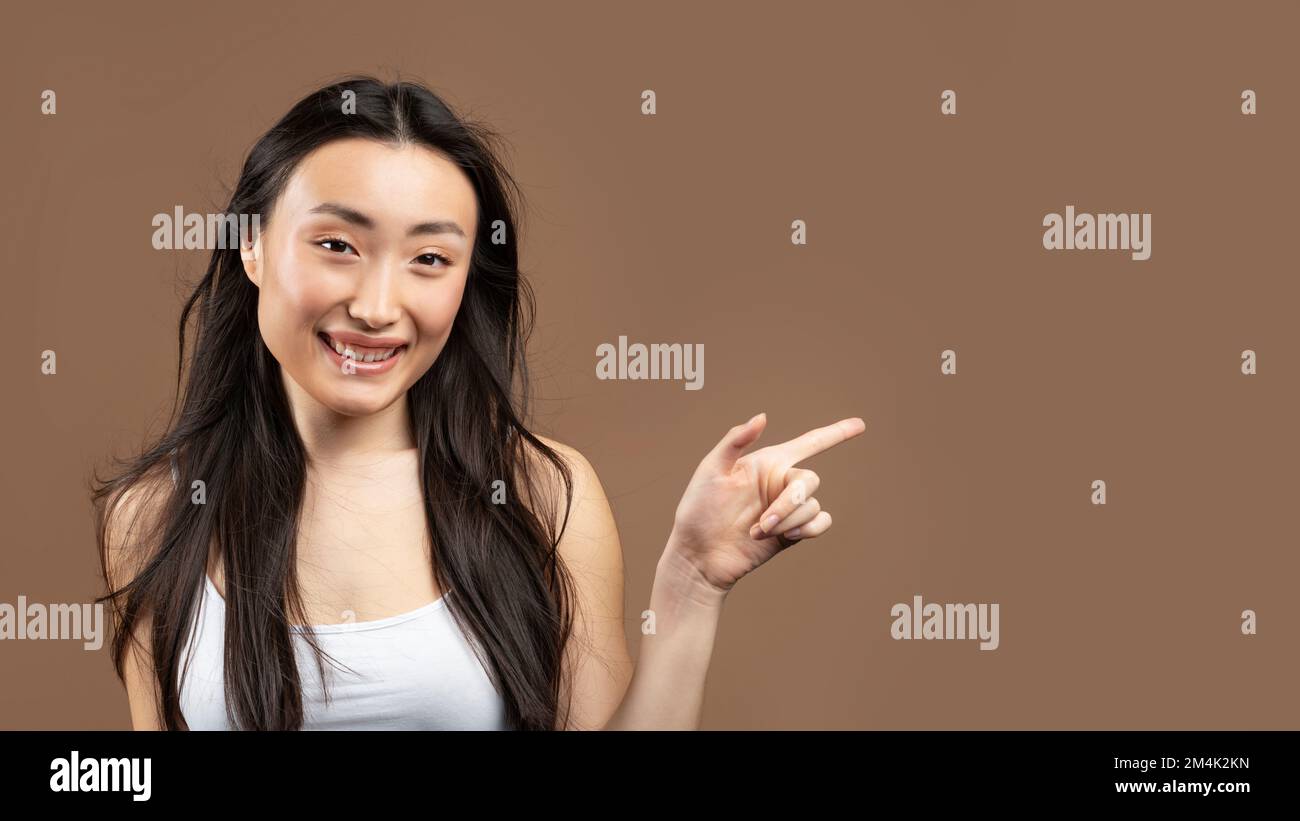 Beautiful young korean lady pointing aside at copy space for text or ...