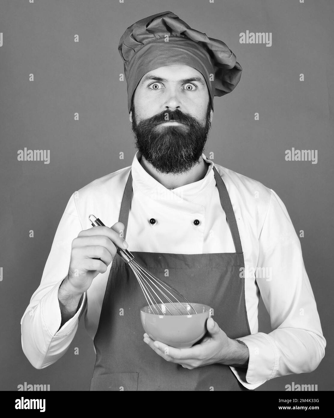 Cook with shocked face in burgundy uniform holds kitchenware Stock ...