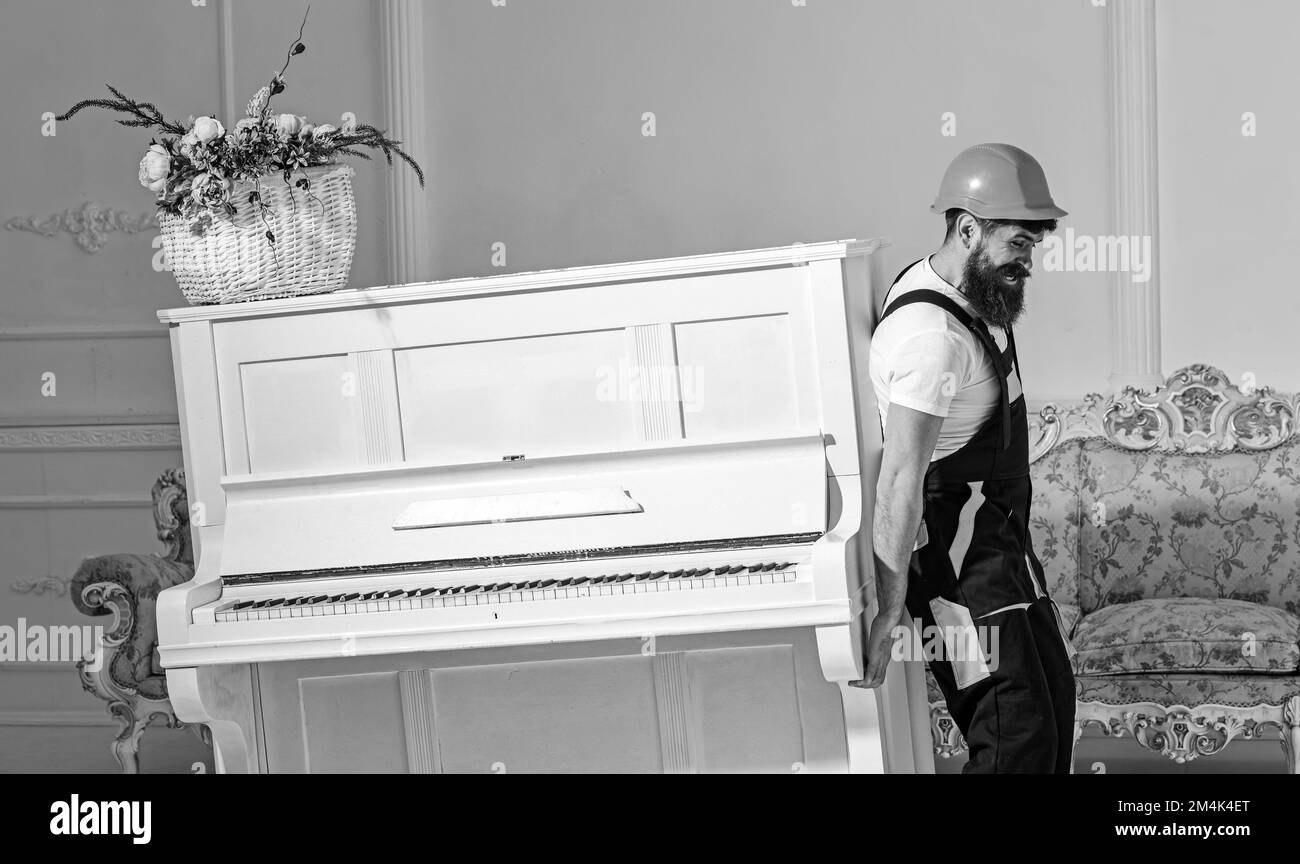 Loader moves piano instrument. Man with beard, worker in overalls and ...