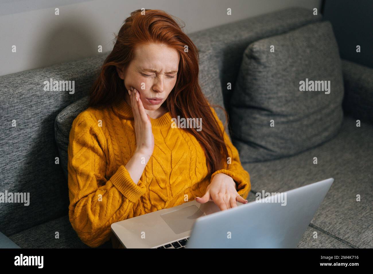 Sad tired young woman having pain in tooth while working typing on ...