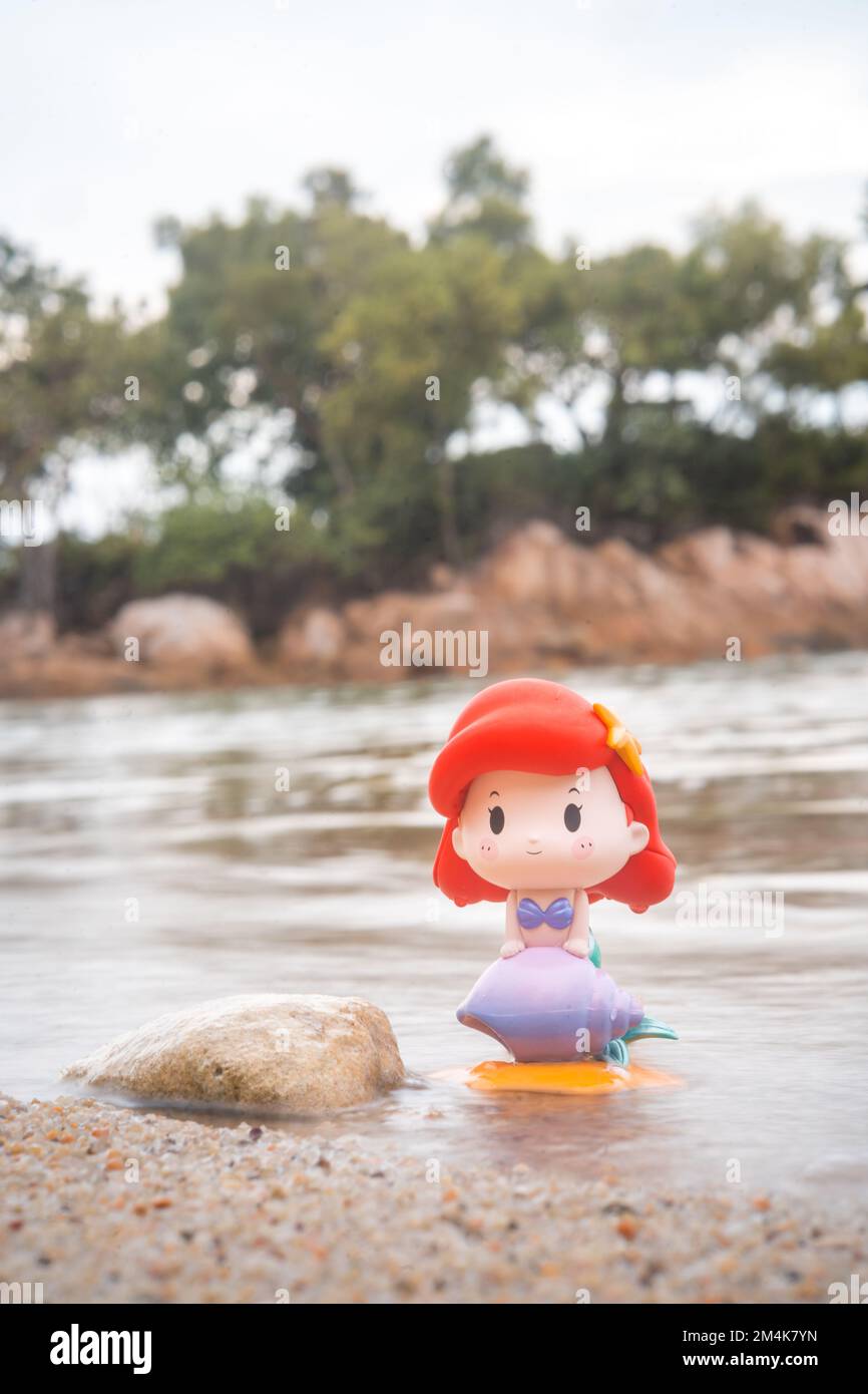A vertical view of POP MART Disney princess Ariel toy on the sand of a ...