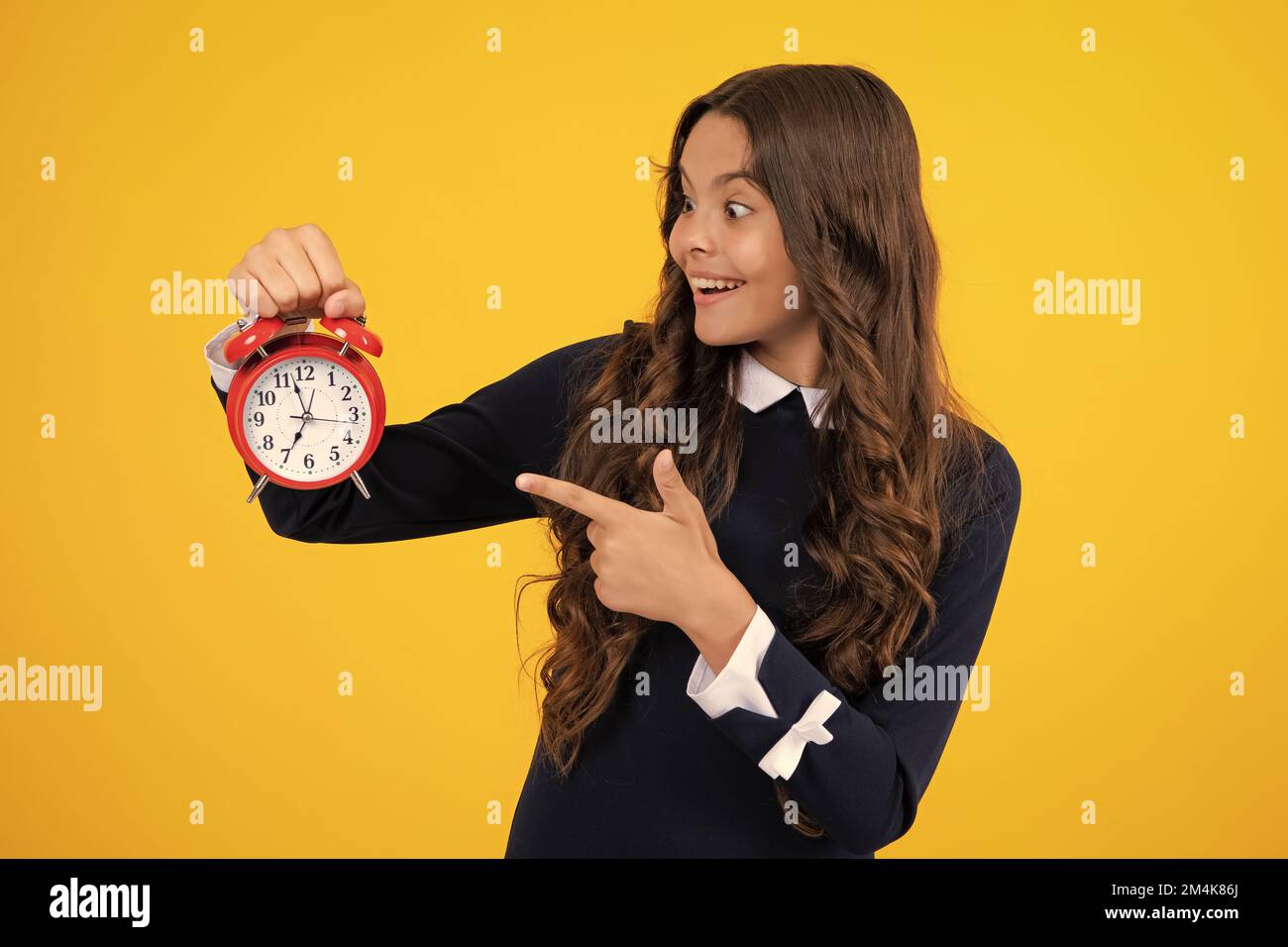 Child teenager girl with alrm clock isolated on yellow background. Time ...