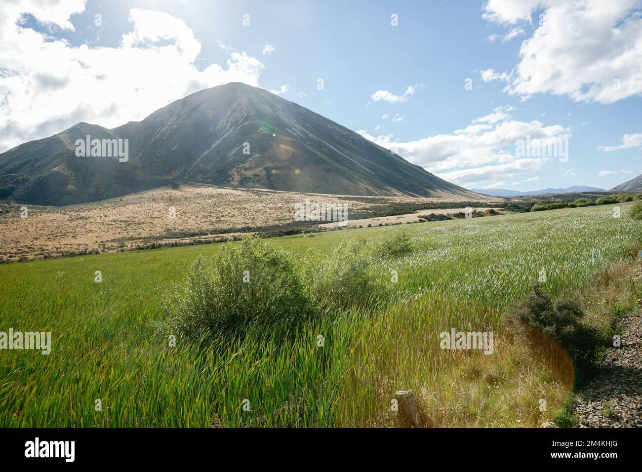 Green sloping field with conical hill in silhouette and sun-flare Stock ...