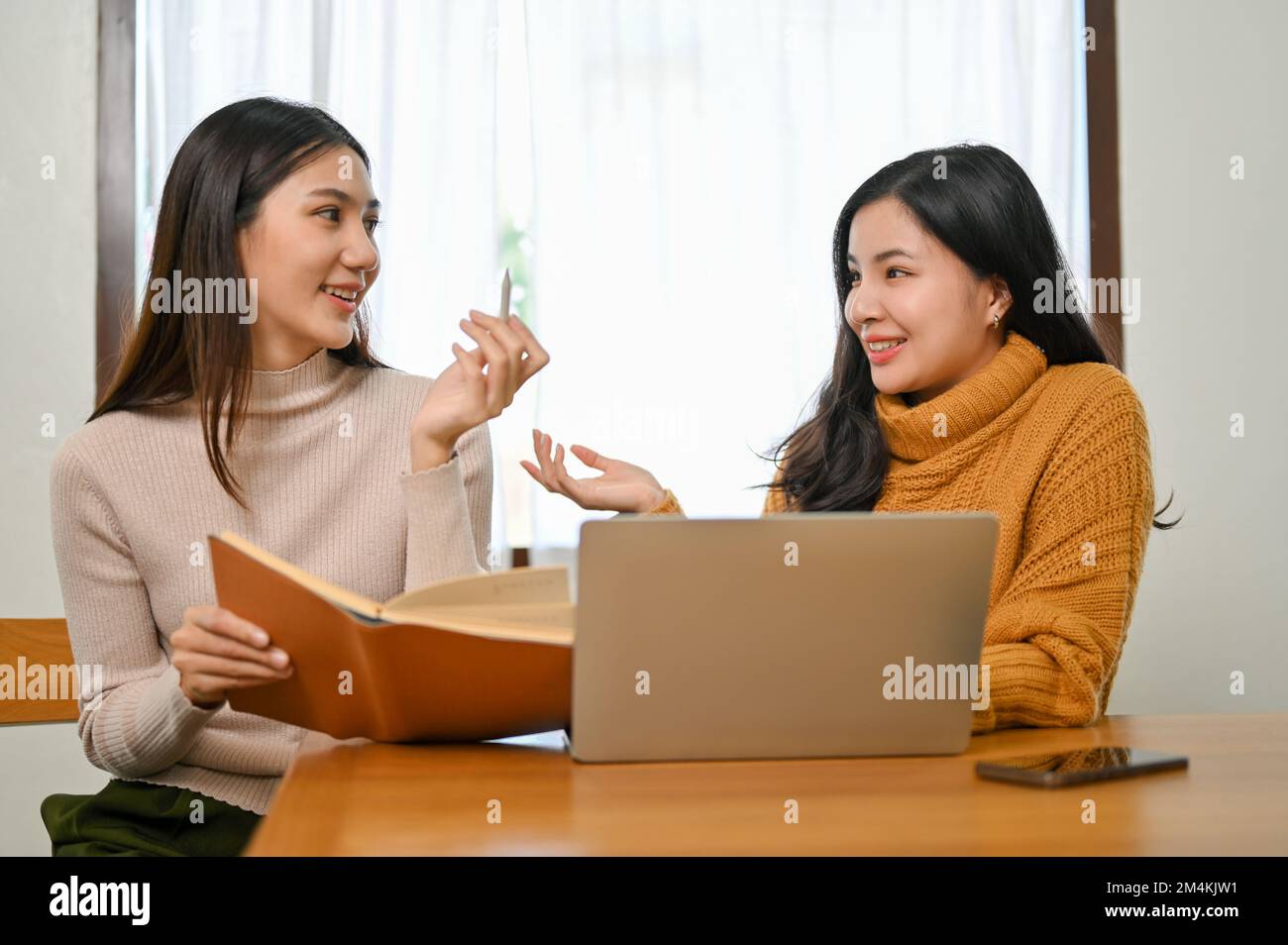 Two pretty Asian female college friends are enjoy talking and ...