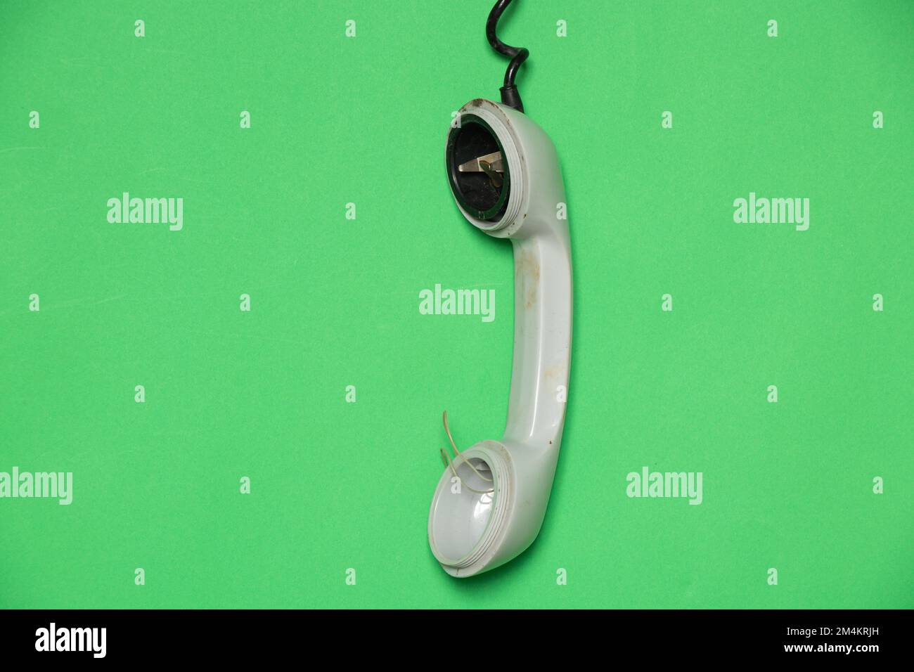 old broken telephone receiver on wire weighs on green isolated ...