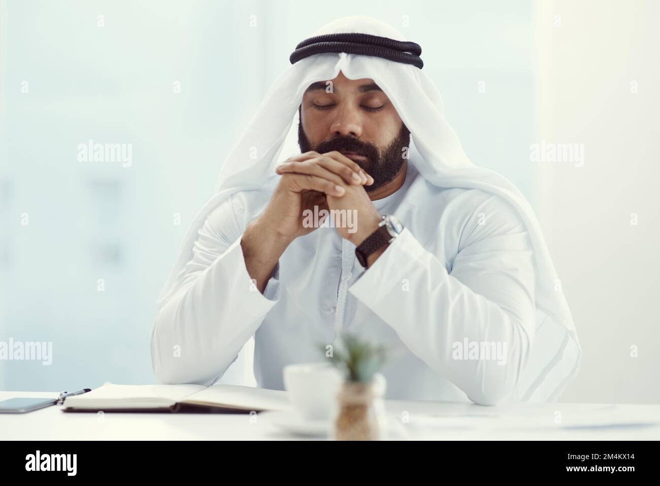 Finding answers through prayer. a young businessman dressed in Islamic ...