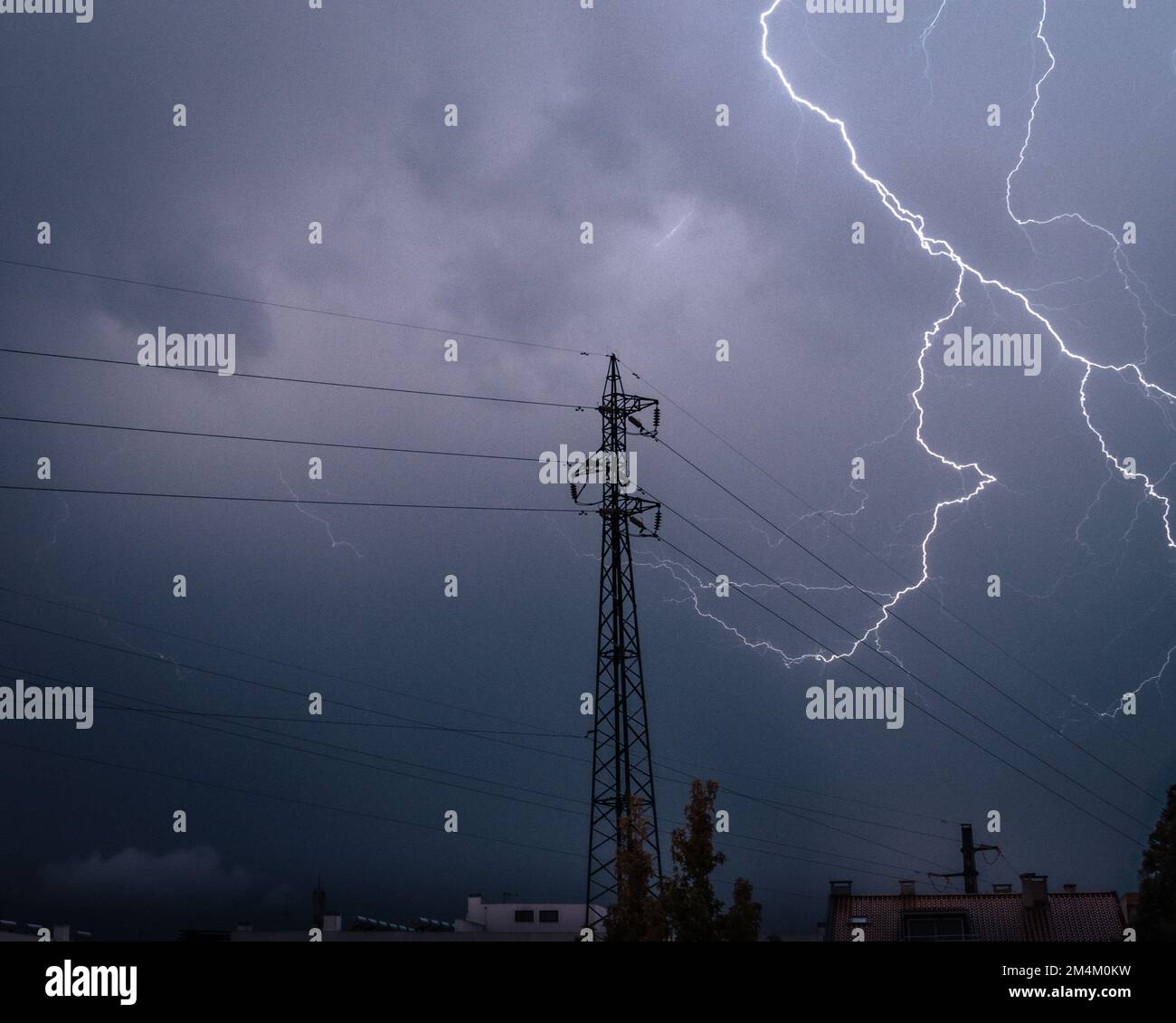 The lightning striking above a transmission tower on a dark gloomy and ...
