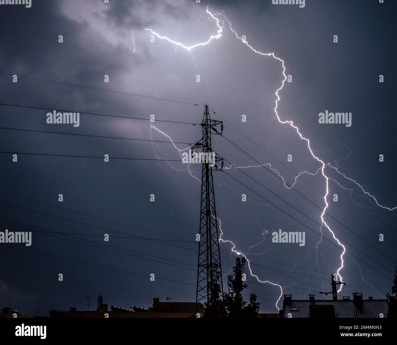 The lightning striking above a transmission tower on a dark gloomy and ...