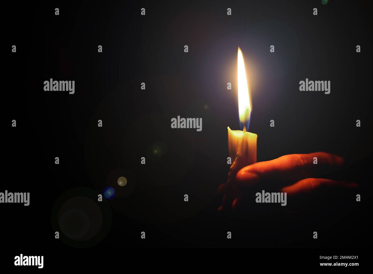glare from a candle flame illuminates a woman's hand in a dark room ...