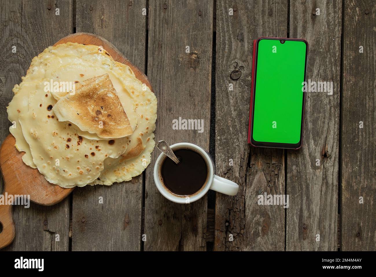 a stack of fried pancakes on a table and a cup with coffee and a phone ...