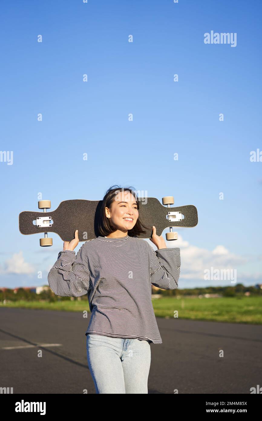 Vertical shot of carefree asian girl with longboard. Young woman skater ...