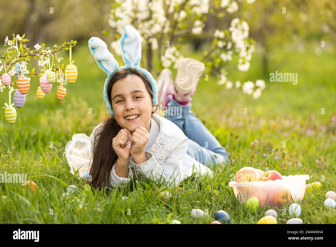 little girl wearing bunny ears with colorful Easter eggs outdoors on ...