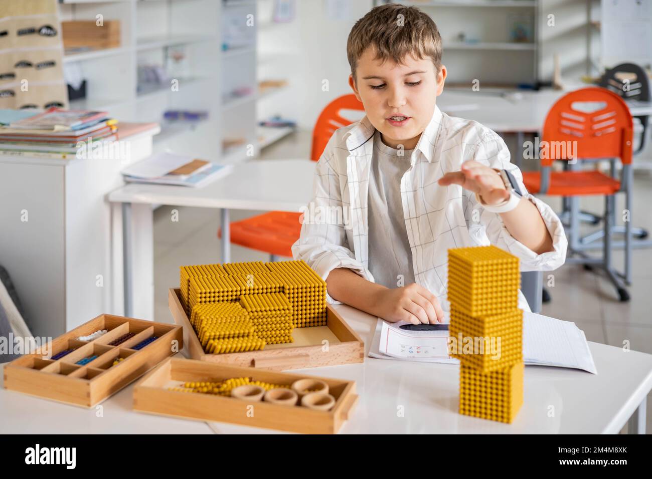 Smiling male kid with Montessori math golden bank material beads ...