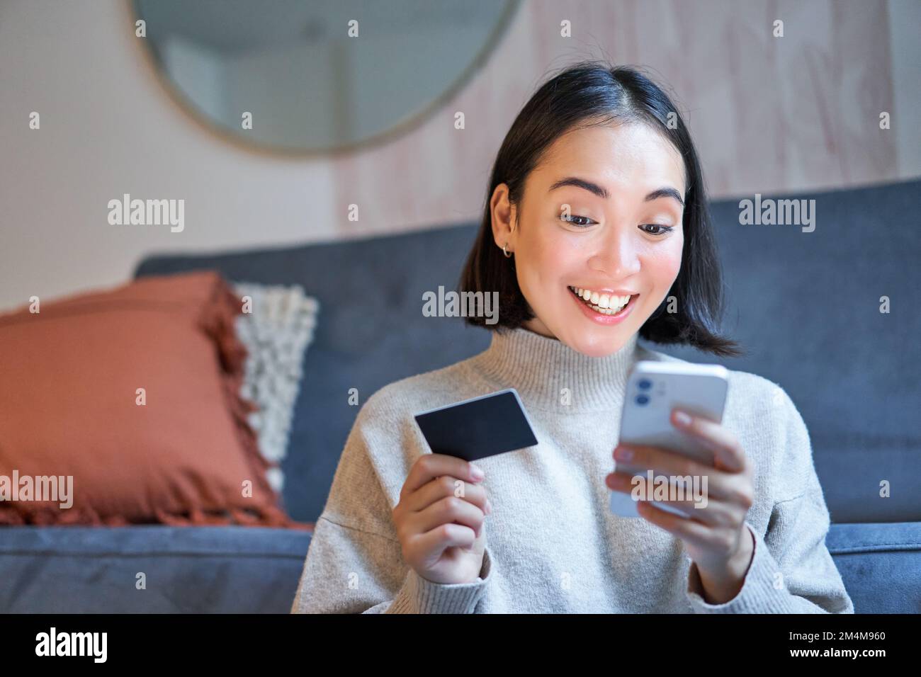 Portrait of smiling asian woman paying with credit card on her smartphone app, arrange direct ...