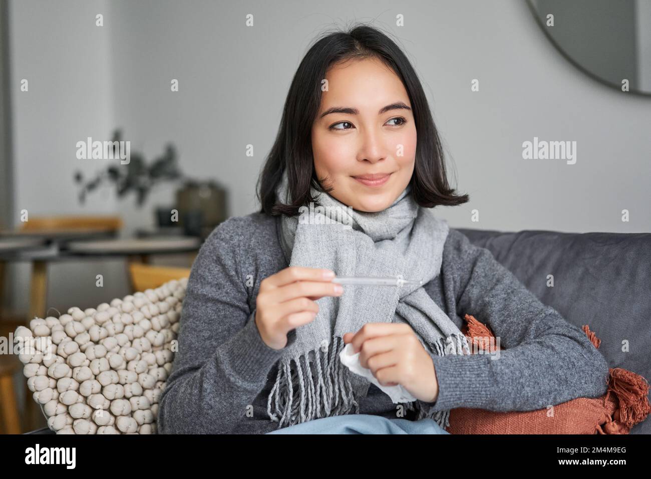 Smiling asian woman holding thermometer and looking pleased, feeling ...
