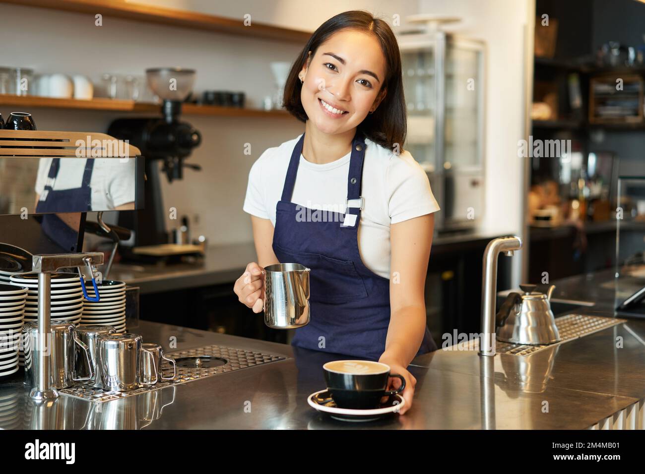 Beautiful young female barista, making cappuccino, pouring steamed milk ...