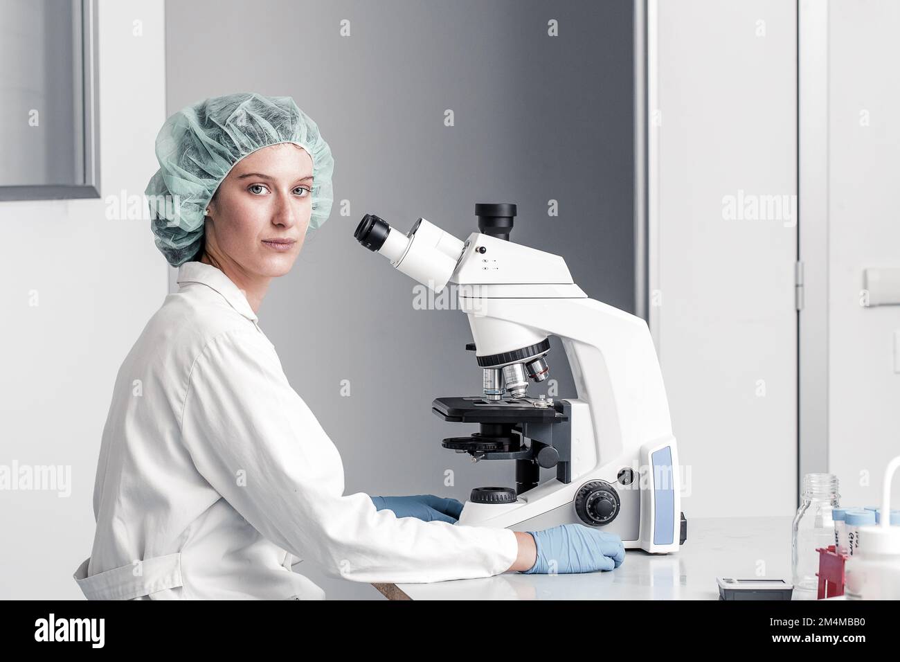 Softly tinted posed portrait of a female scientist under a microscope ...