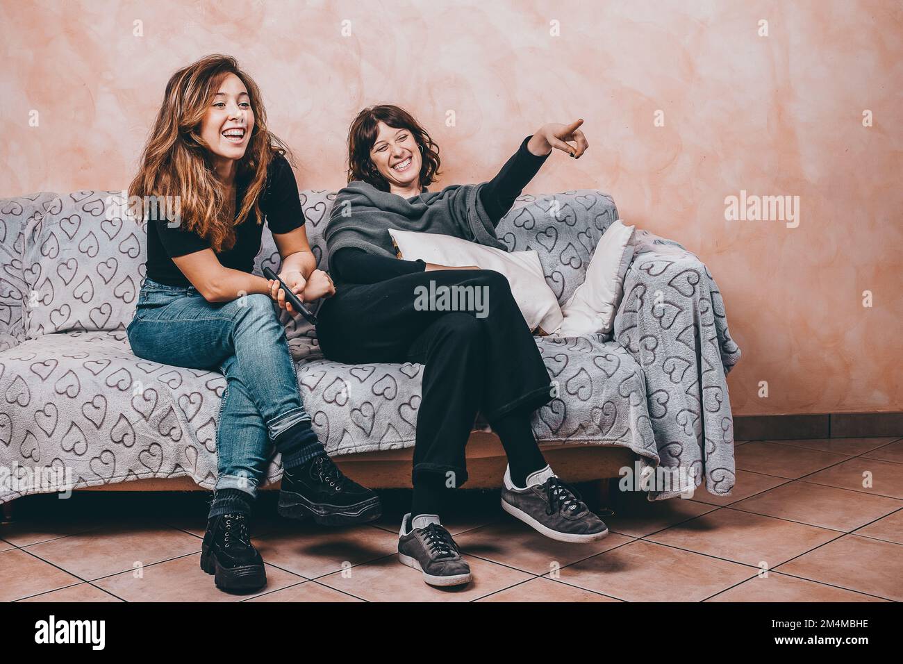 Two young girlfriends sitting on the couch laughing while watching ...