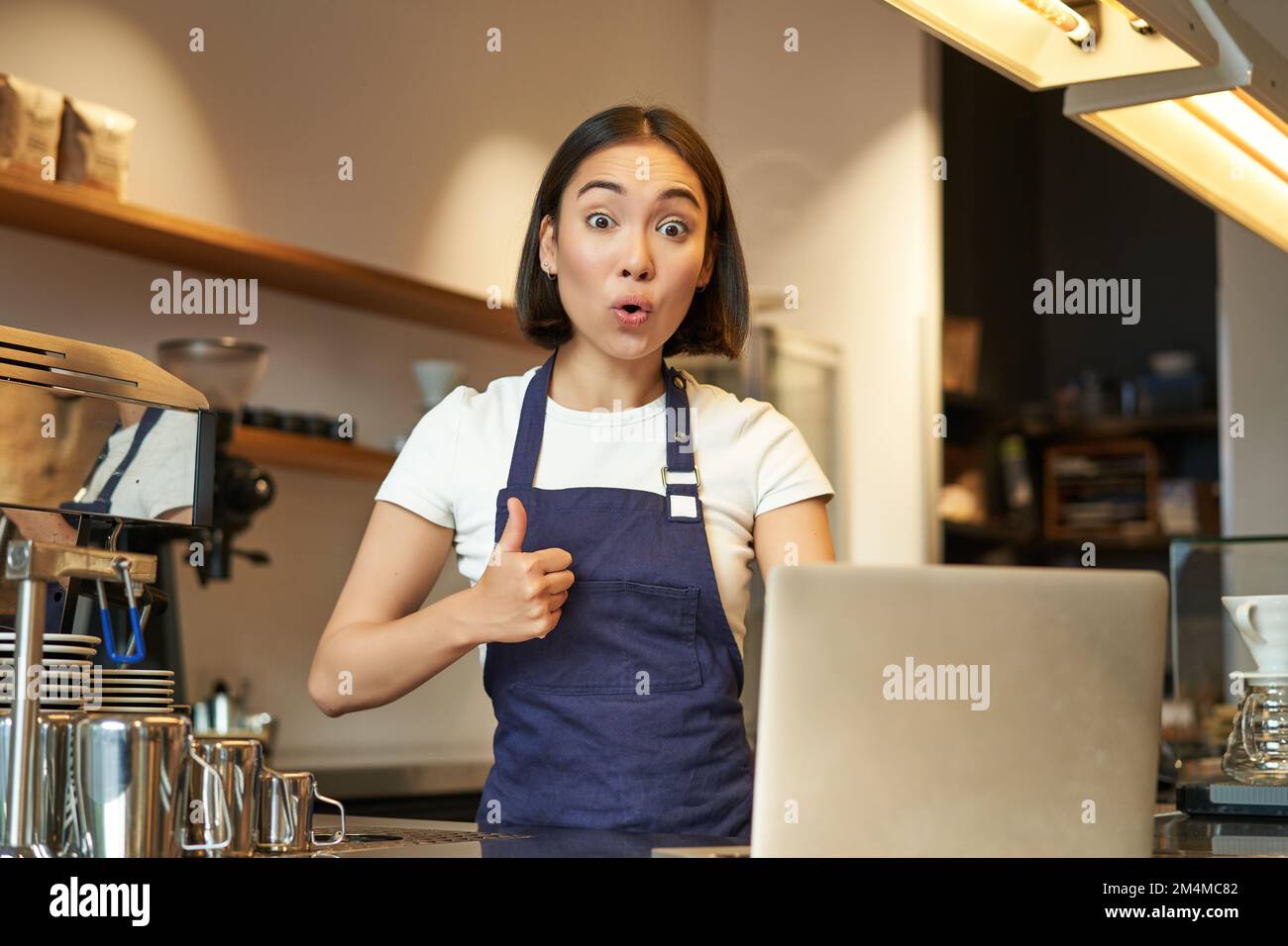 Surprised barista girl, female coffee shop worker shows thumbs up ...