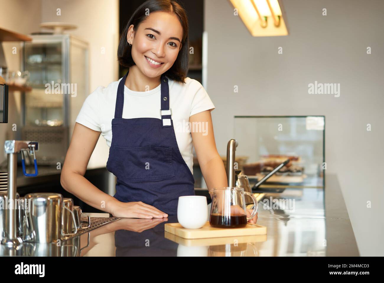Smiling beautiful barista girl in apron, making batch brew, filter ...