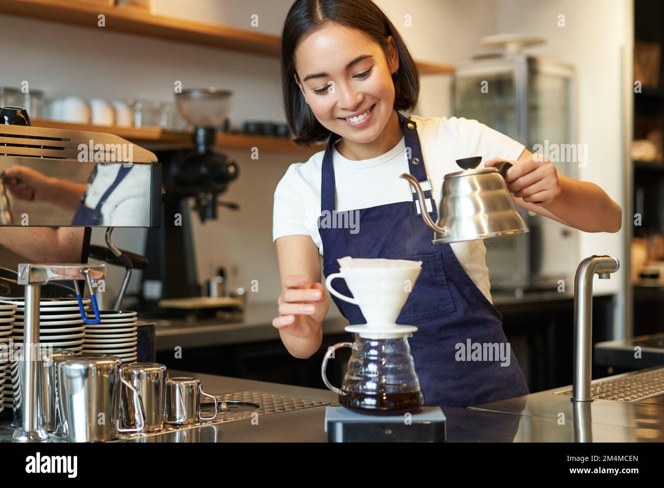 Cute brunette girl barista, cafe staff pouring water from kettle and ...