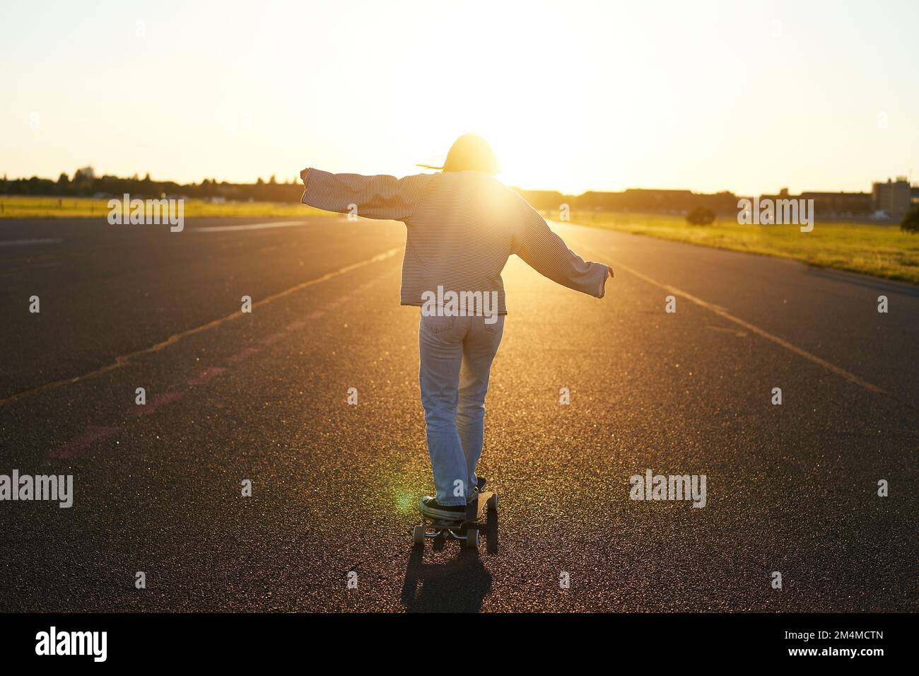 Rear view photo of young girl riding skateboard towards sunlight. Happy ...