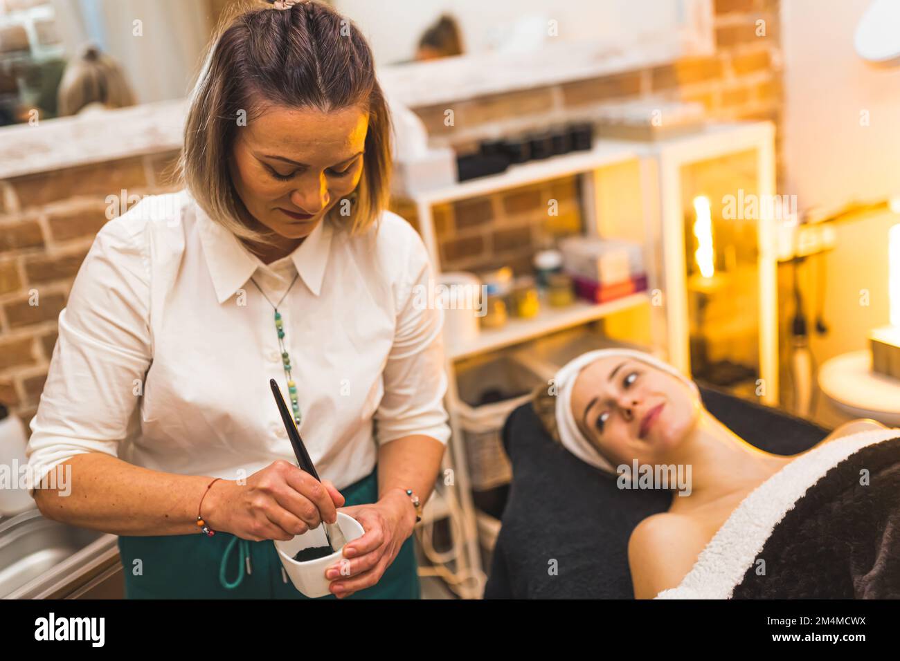 Mid adult caucasian woman preparing clay mask for her client's face ...
