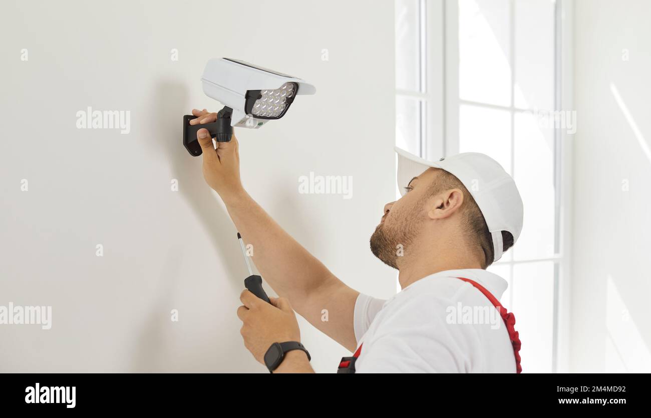 Electrician worker installs and screws video surveillance camera with ...