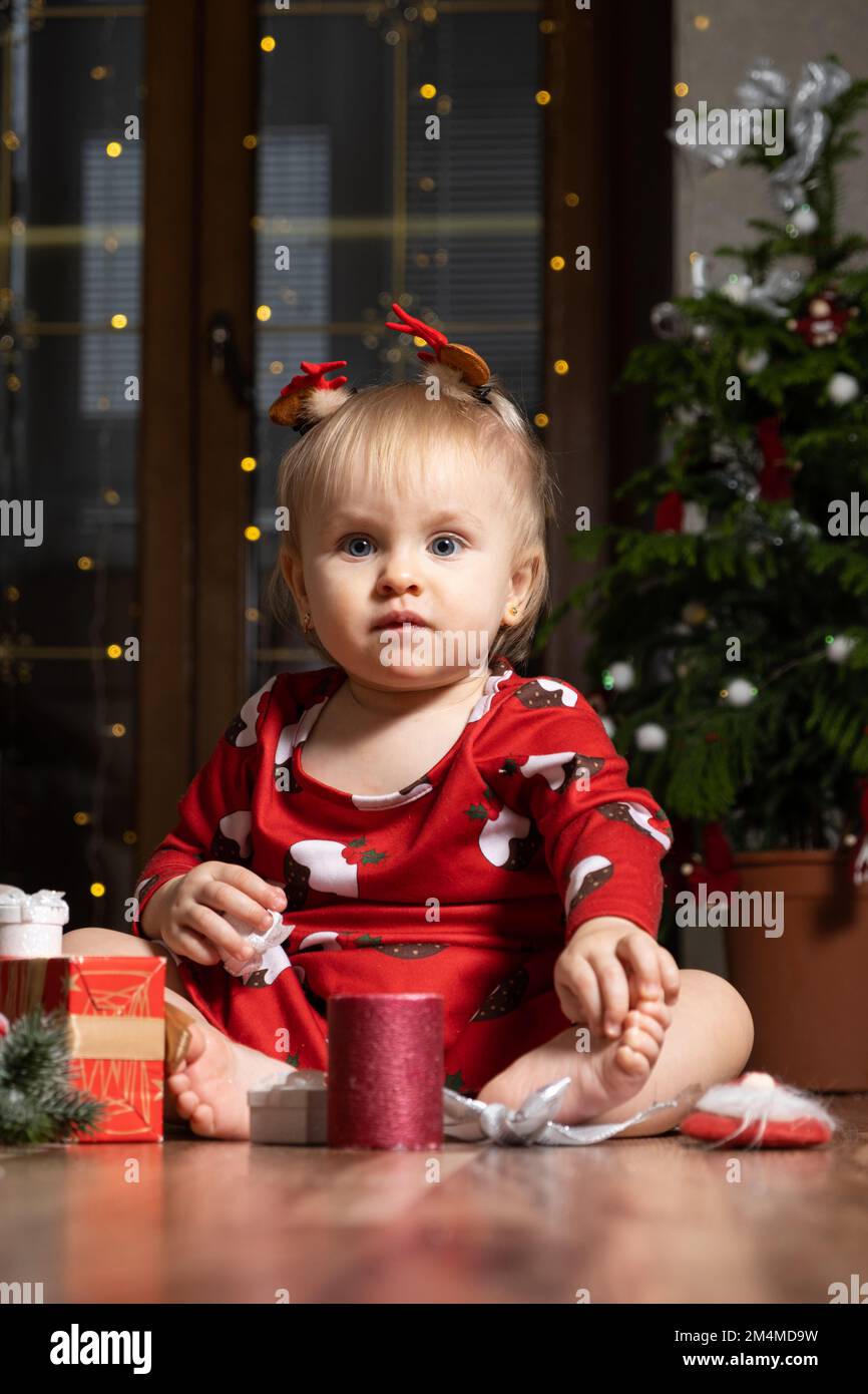 A beautiful little girl sits near a Christmas tree. Winter holidays and ...