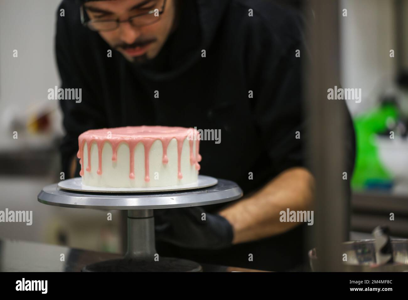 cake chef designer preparing a pink dripping on white frosted cake for ...