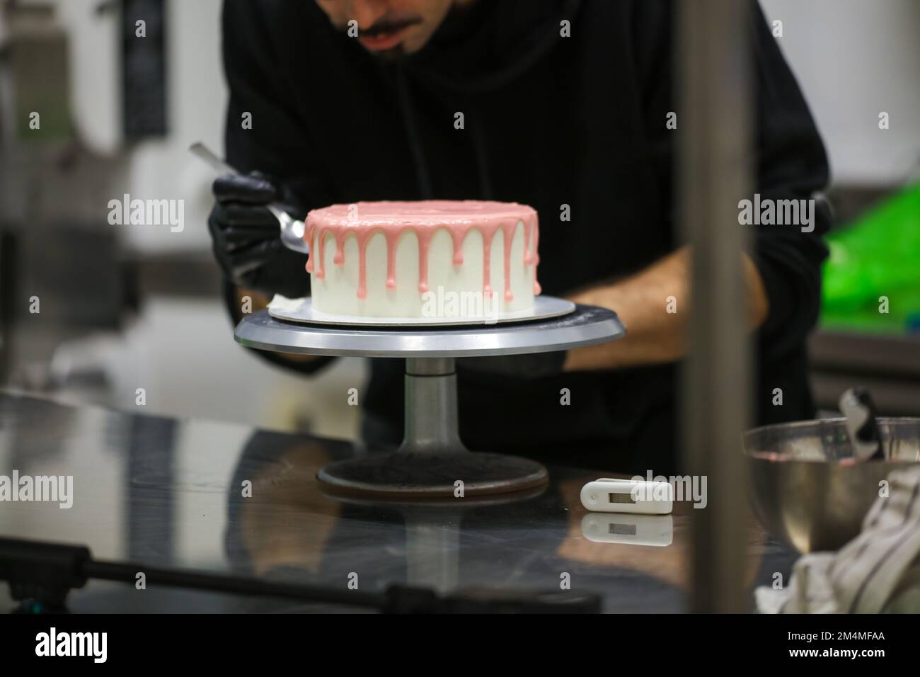cake chef designer preparing a pink dripping on white frosted cake for ...