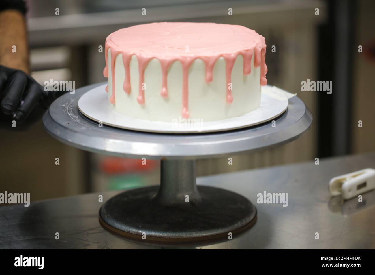 cake chef designer preparing a pink dripping on white frosted cake for ...