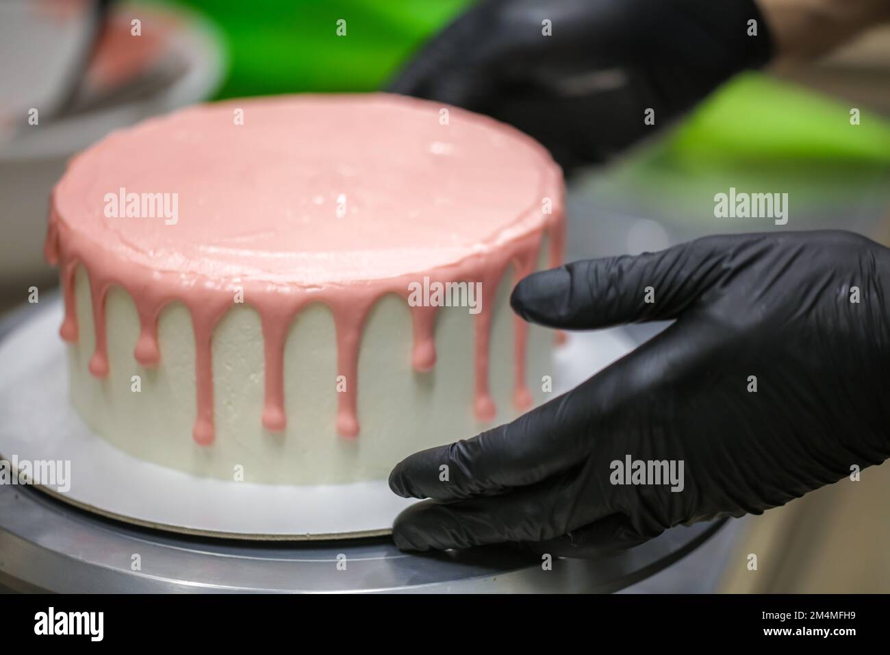 cake chef designer preparing a pink dripping on white frosted cake for ...