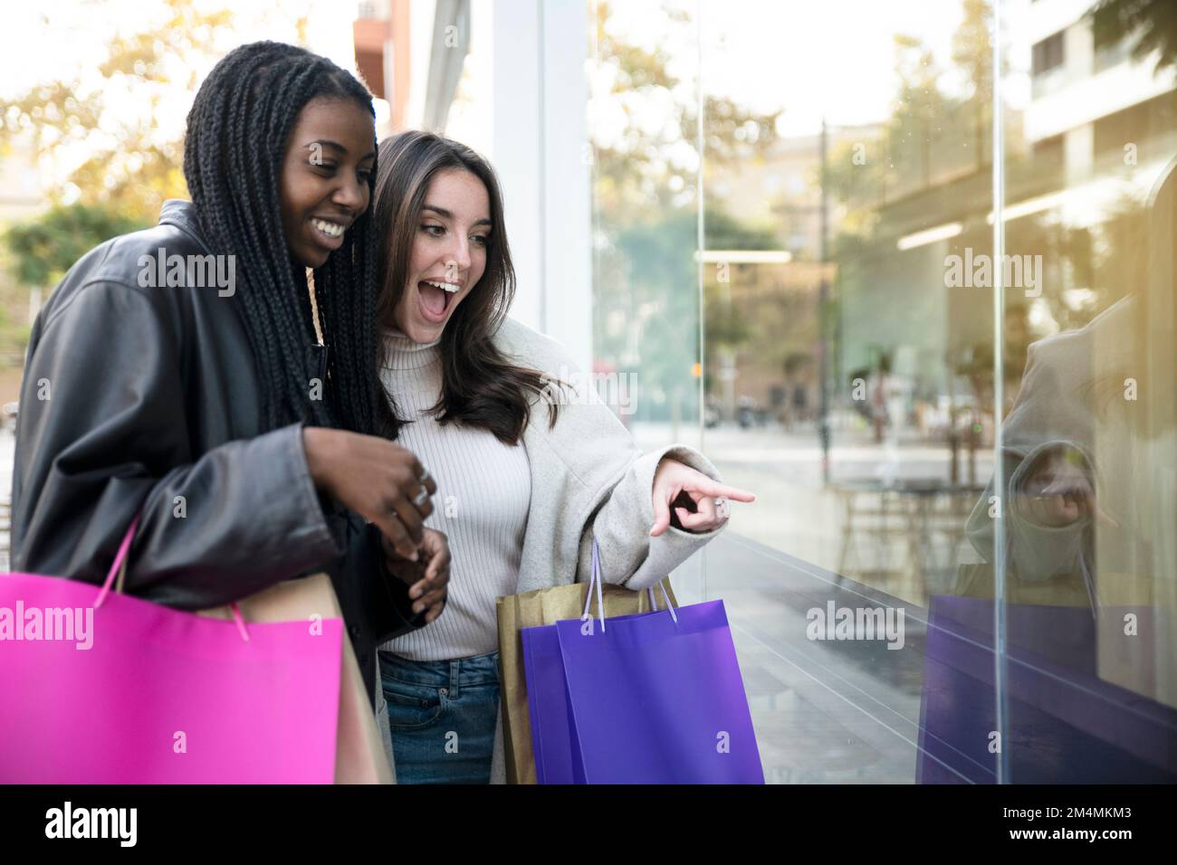 Happy young women with shopping bags looking to shop window - sale ...