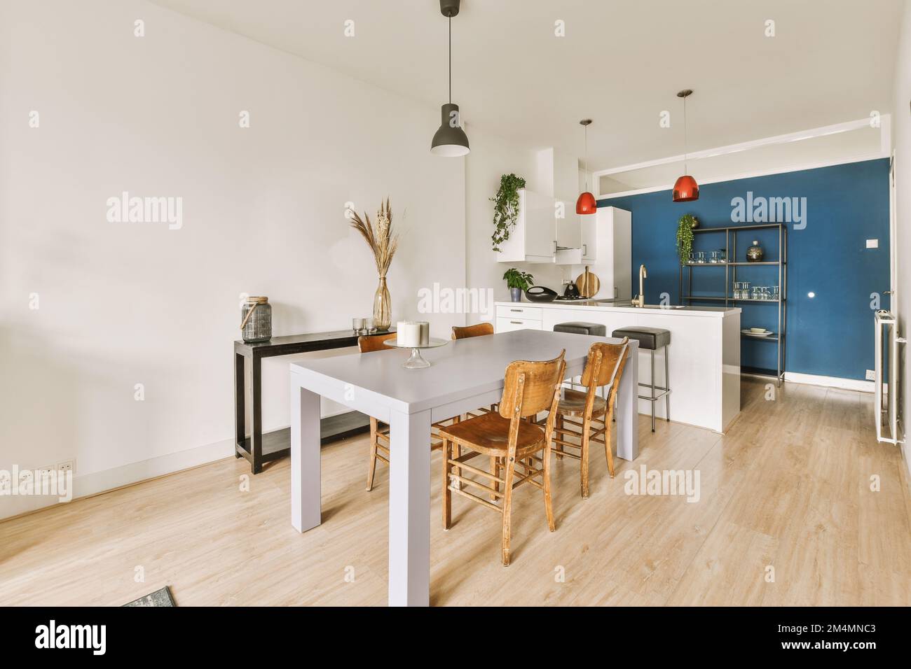 a dining room with wood flooring and blue accent wall behind the table is an open kitchen area ...